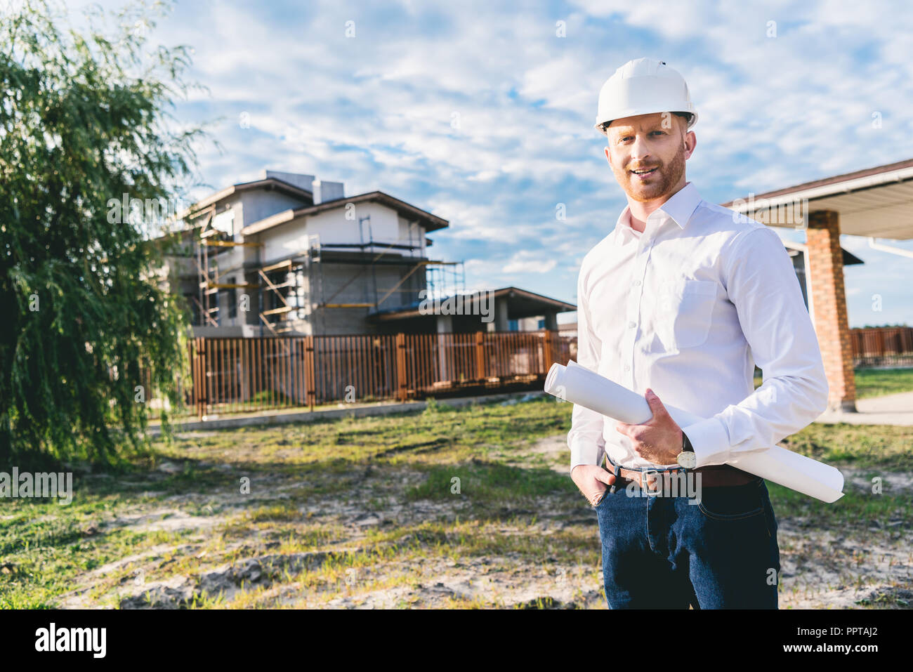 handsome architect in white shirt with blueprint standing at yard in ...