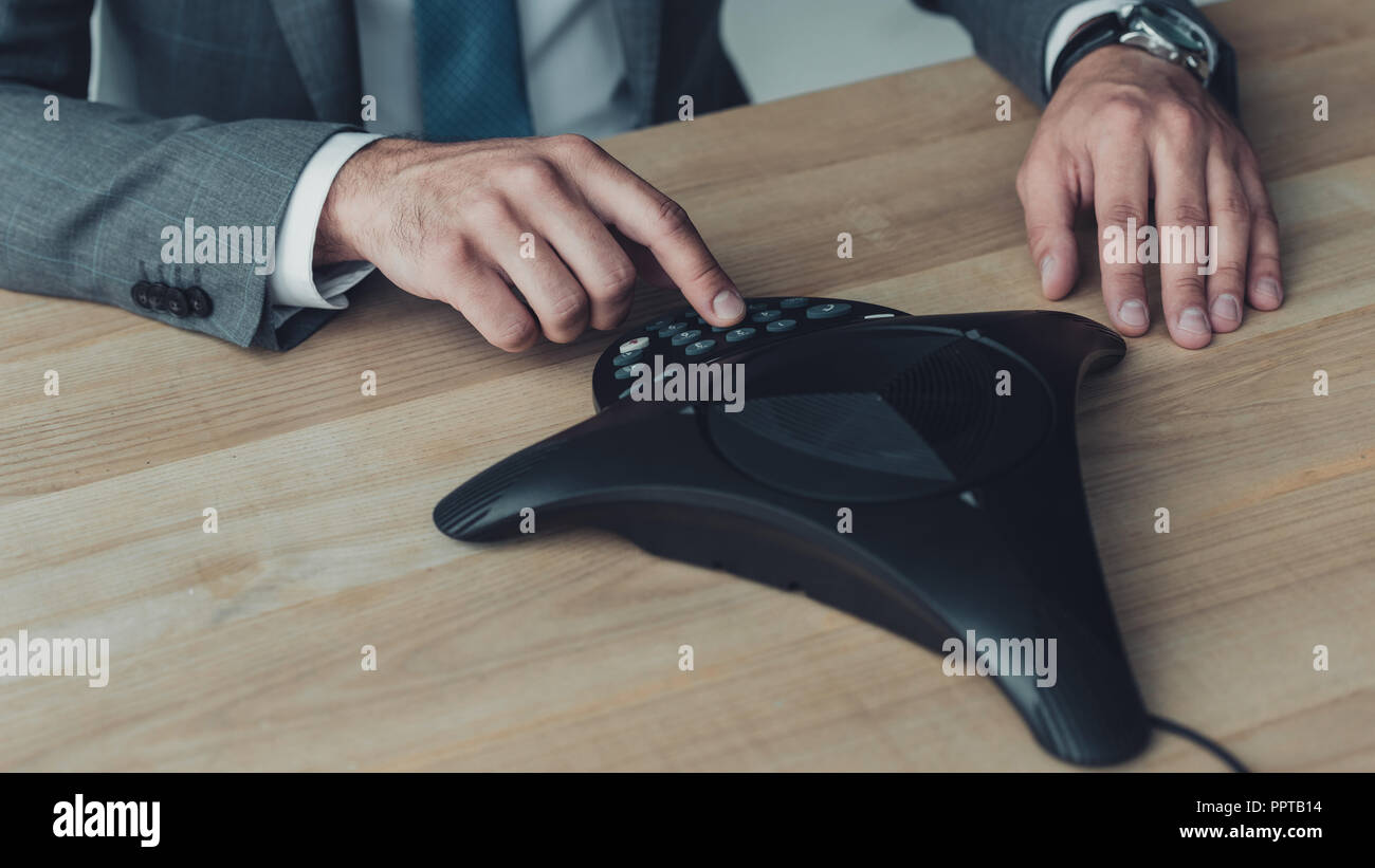 cropped shot of businessman pushing button of speakerphone at workplace ...