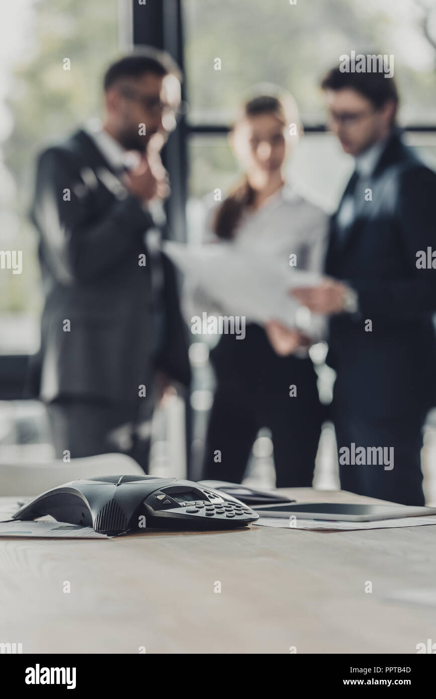 close-up shot of conference phone with blurred business people working ...