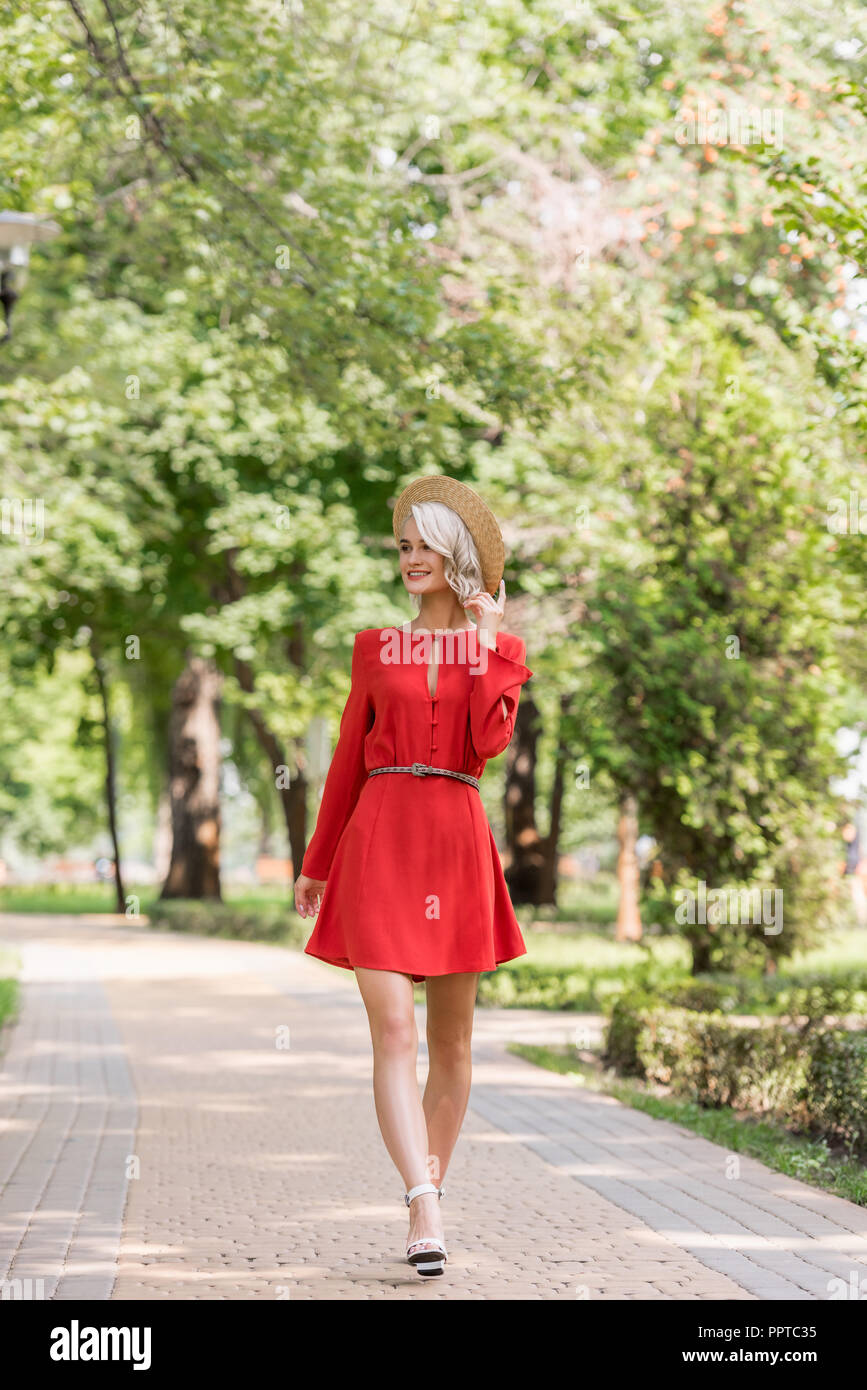 smiling beautiful girl in red dress and straw hat walking in park and ...