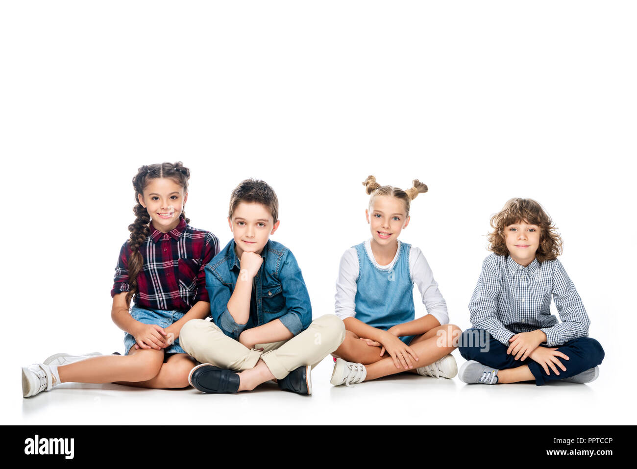 four schoolchildren sitting and looking at camera isolated on white ...