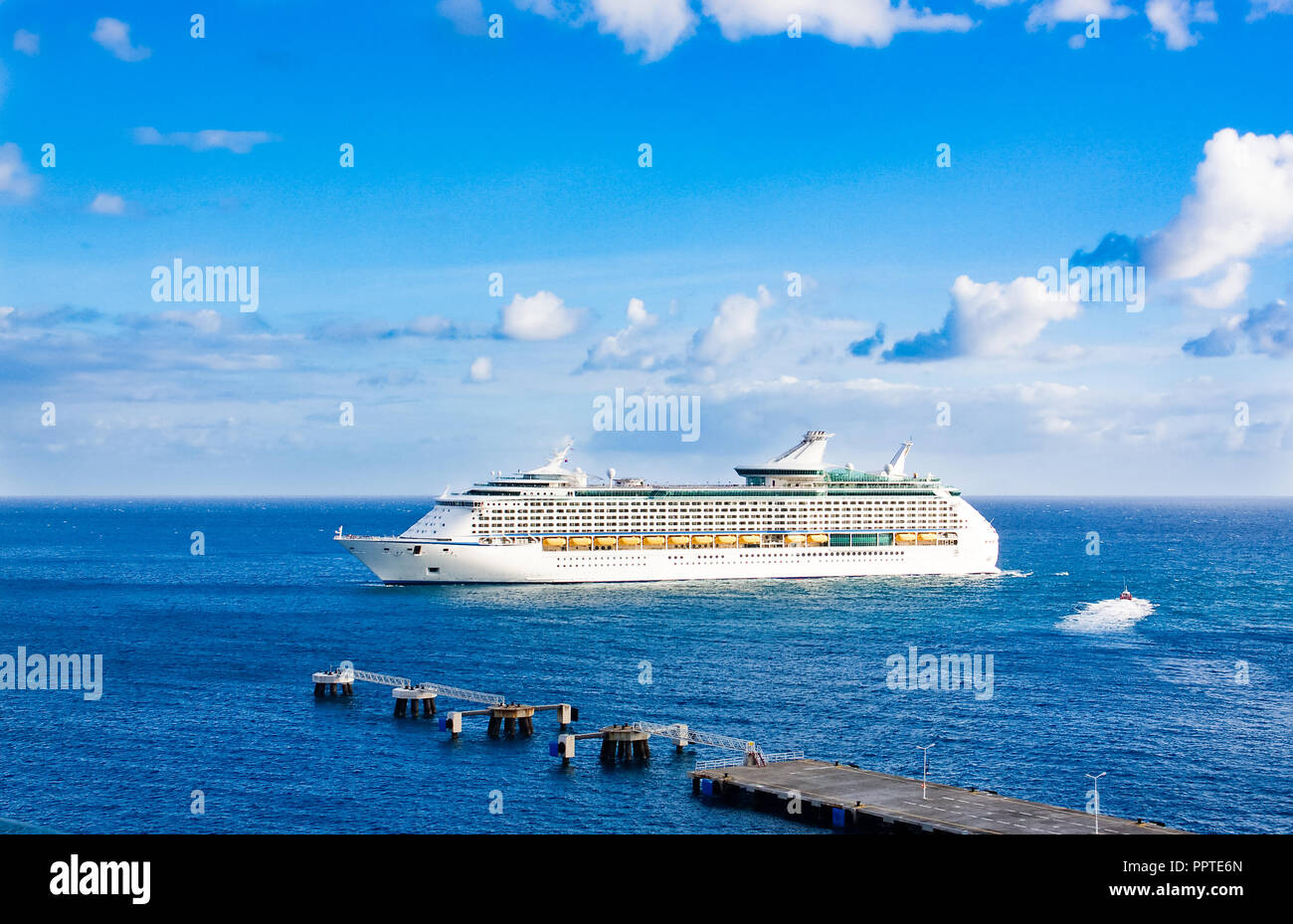 A large luxury cruise ship with a red pilot boat in deep blue water ...