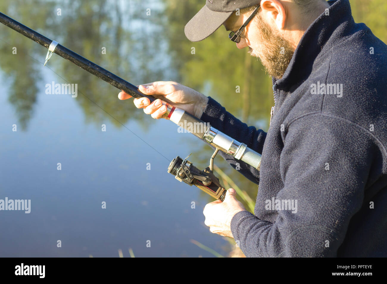 The angler in the hat stands with a fishing rod over the water and ...