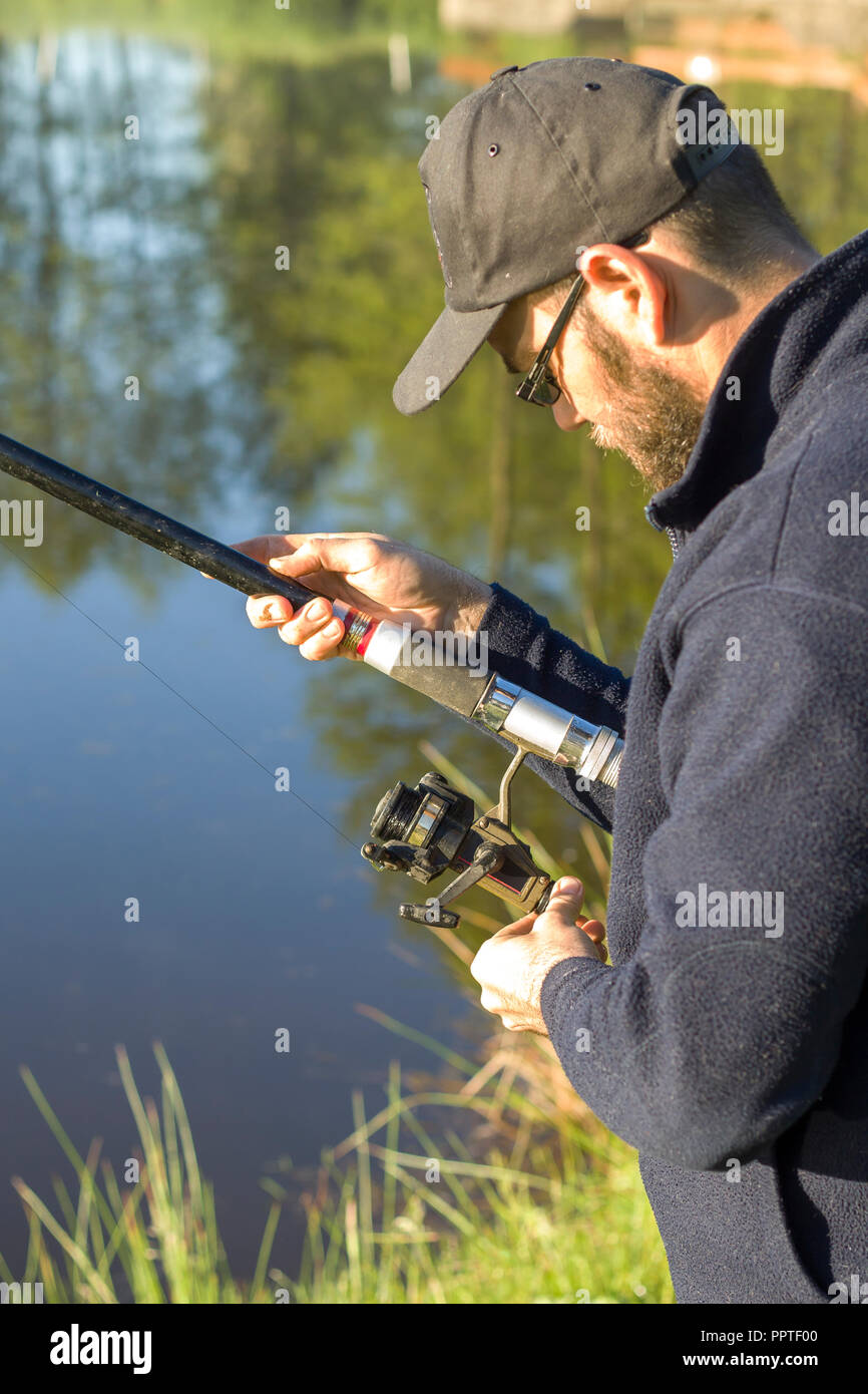 The angler in the hat stands with a fishing rod over the water and ...