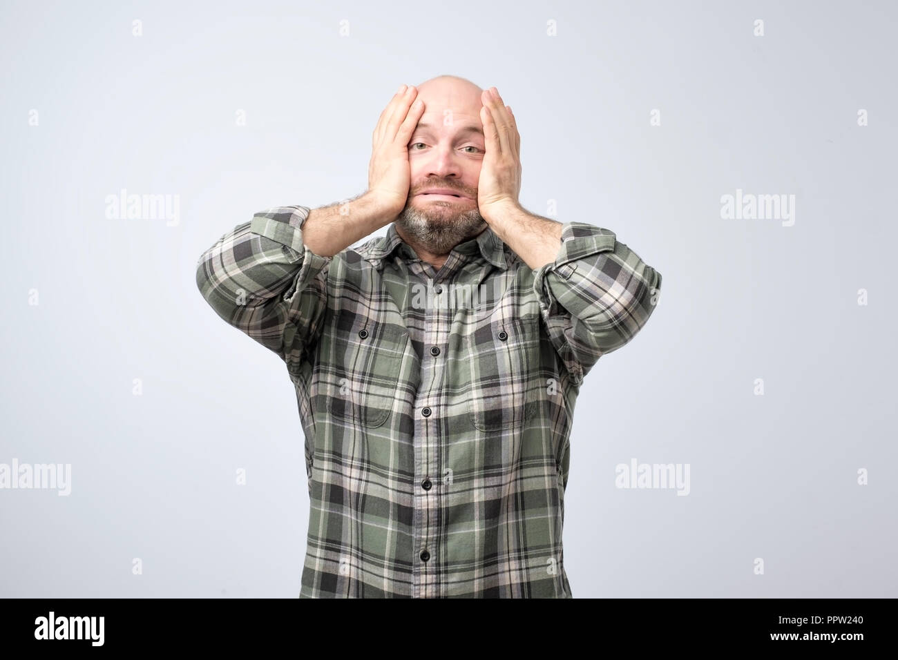 Mature annoyed man pulling skin on face with hands. He is scared or ...