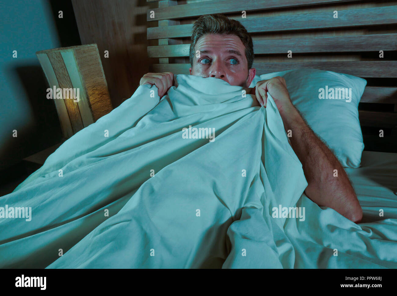 sleepless young man lying in bed stressed and scared suffering ...