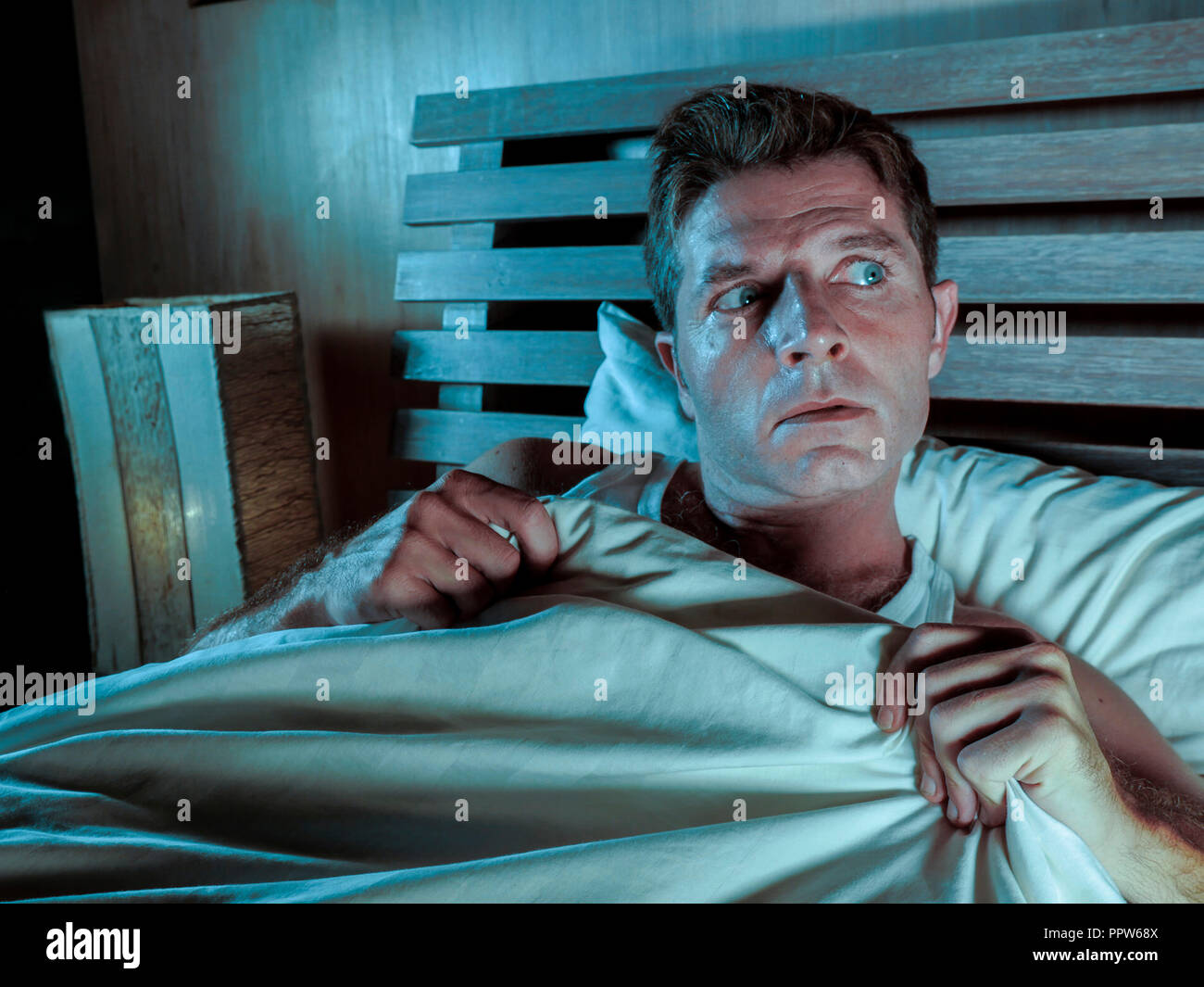 sleepless young man lying in bed stressed and scared suffering nightmare and horror bad dream ...