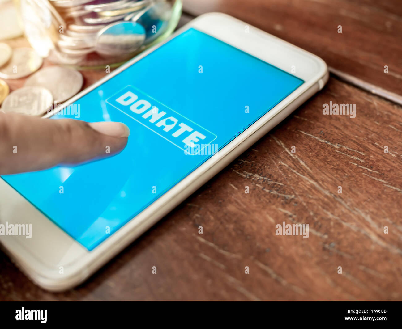 Finger pressing donate icon button on blue screen on white mobile phone ...