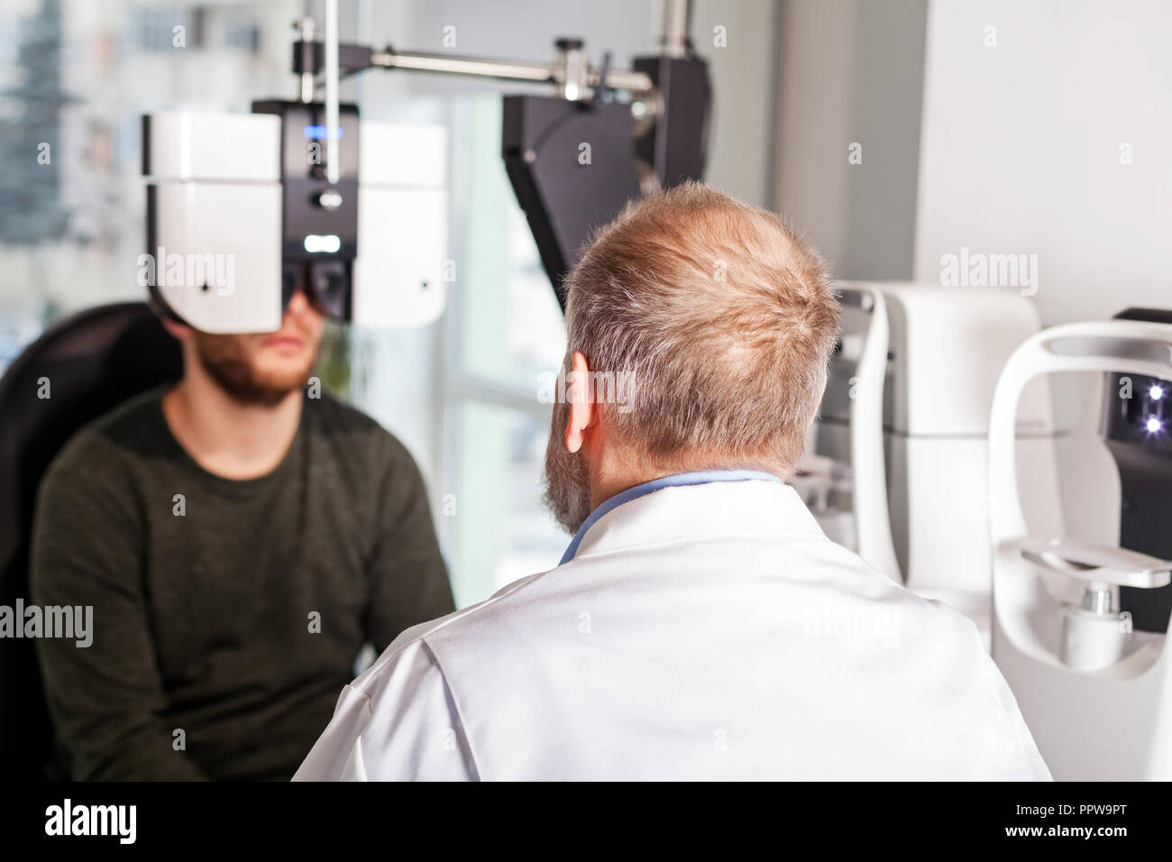 Ophthalmologist examining young man with optometric machine in optics ...