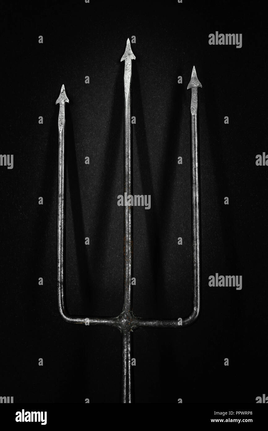 Old, rusty and metal trident casting the shadow on black background ...