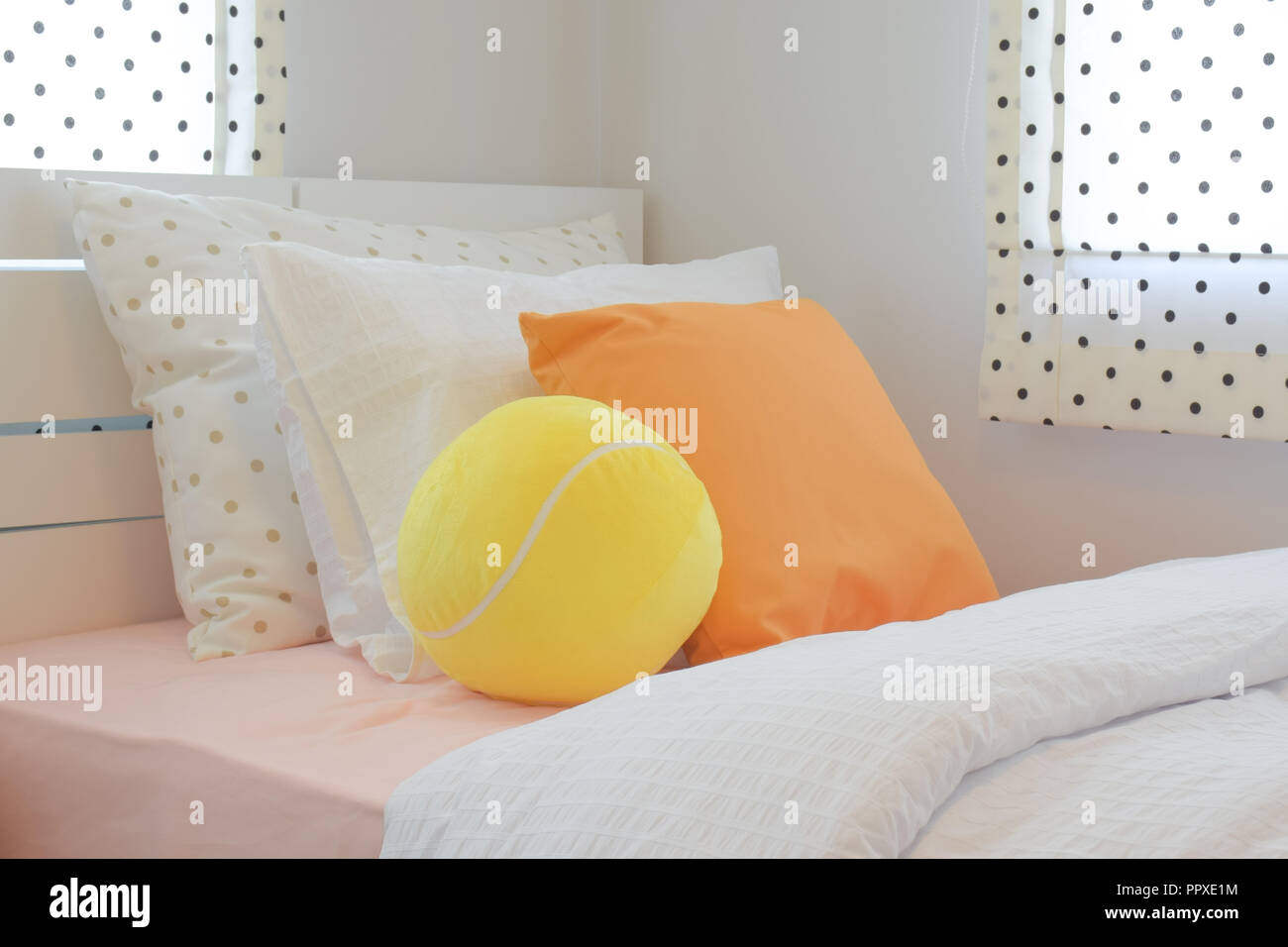 Yellow puffy ball and orange color pillow on bed in sweet color scheme ...