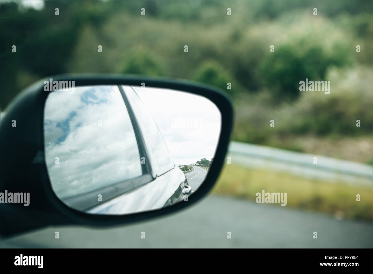 A close-up of a car rear view mirror while driving on an asphalt road ...