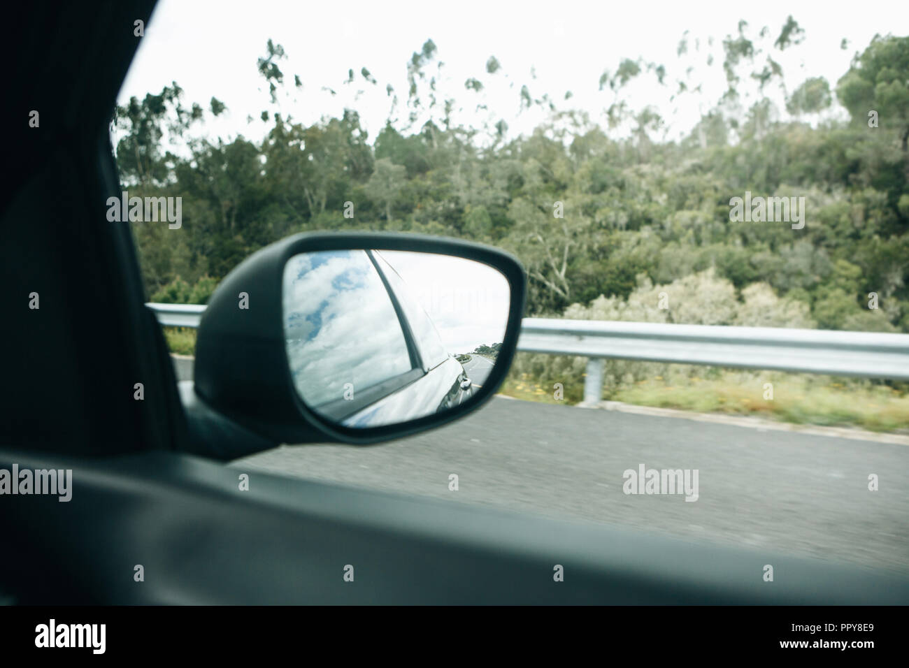 A close-up of a car rear view mirror while driving on an asphalt road ...