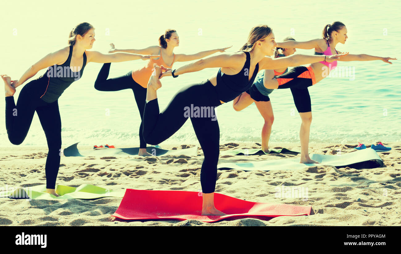 Yoga on sea beach, group of young women exercising asanas Stock Photo ...