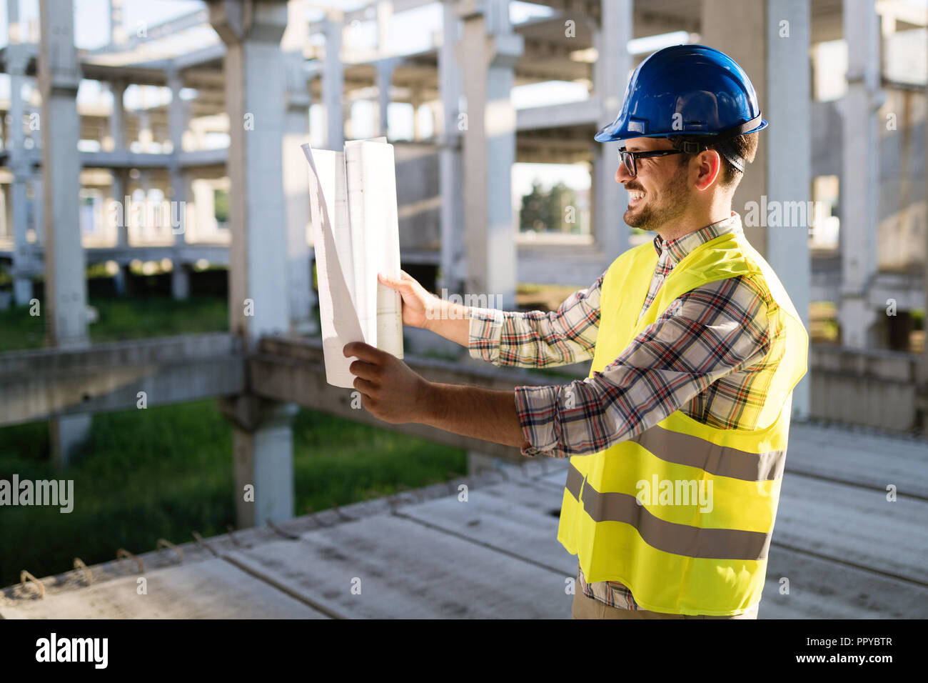 Portrait of male site contractor engineer with hard hat holding blue ...