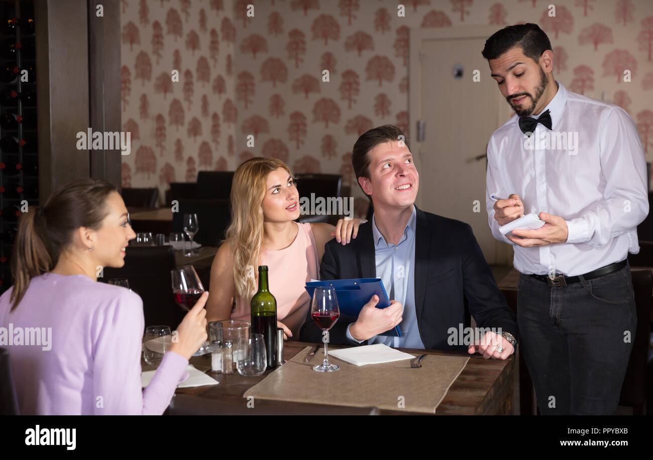Confident waiter helping group of friends with menu, taking order in ...