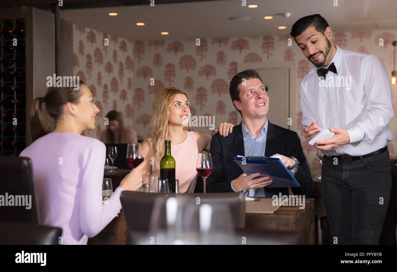 Nice waiter helping group of friends with menu, taking order in ...