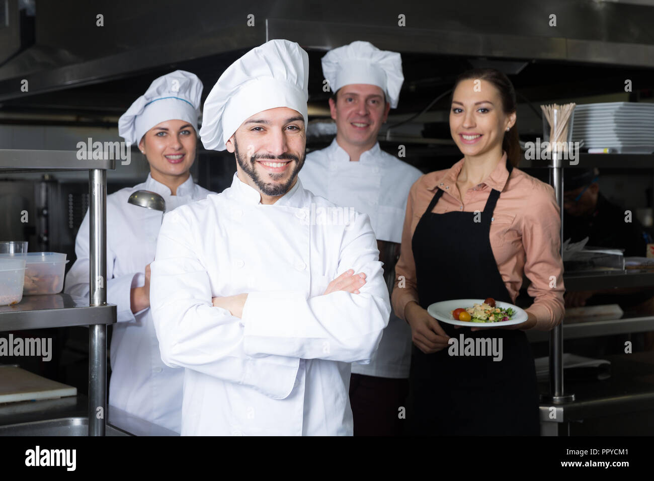 Portrait of confident cheerful chef in kitchen with staff of restaurant ...