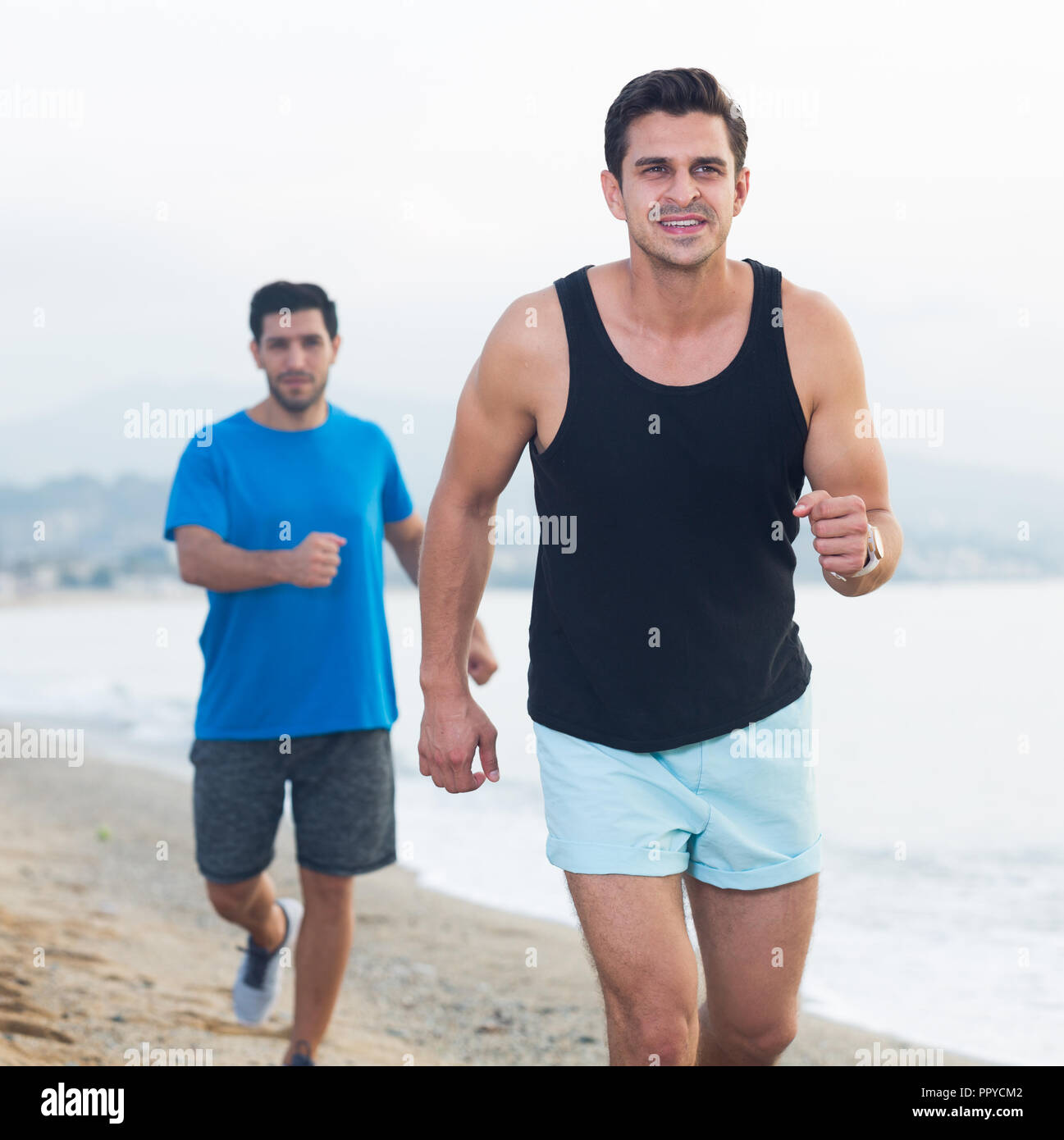 Adult men are jogging together on the beach near ocean Stock Photo - Alamy