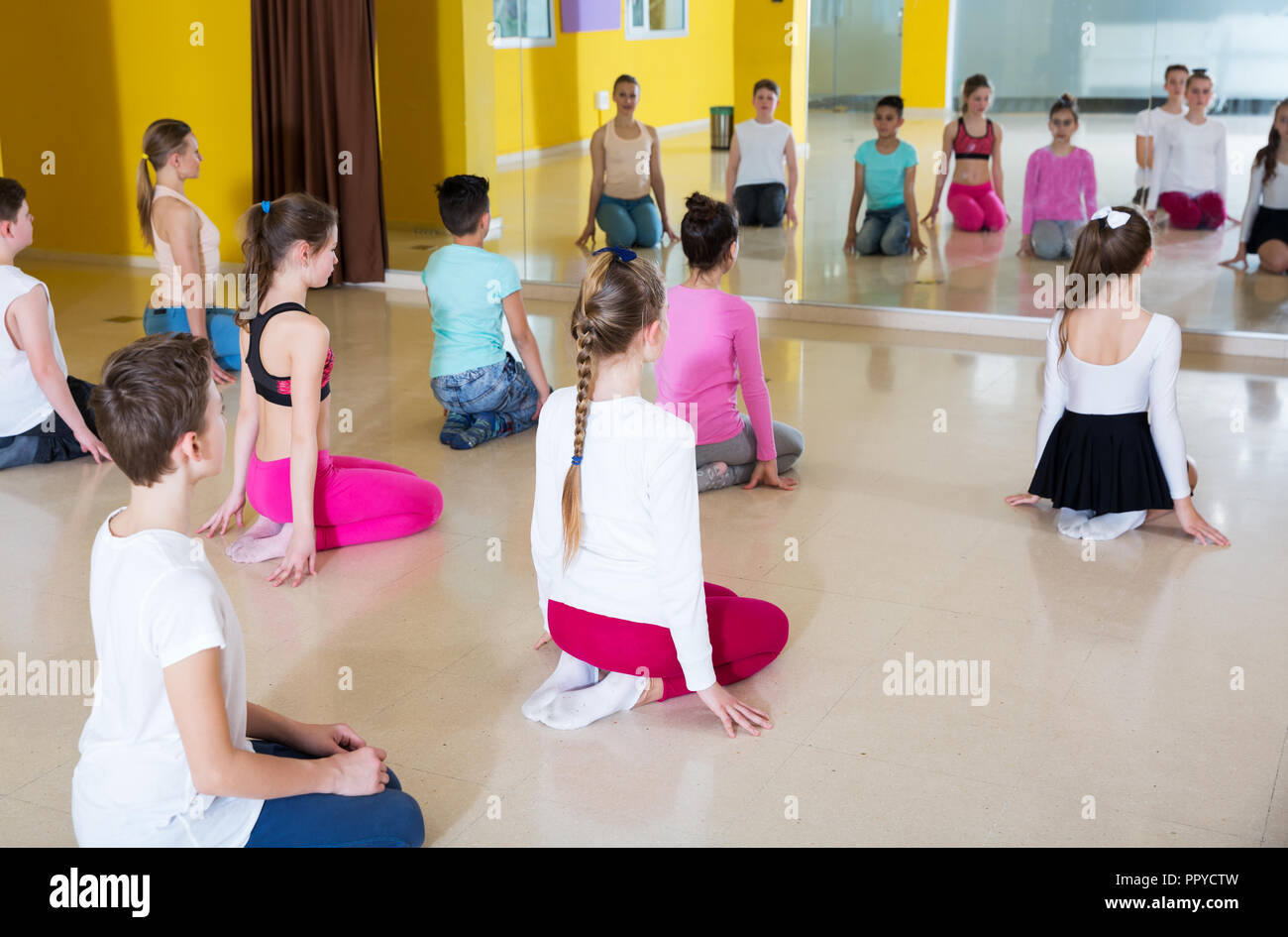 Rear view of group of tweens exercising with female coach in front of ...