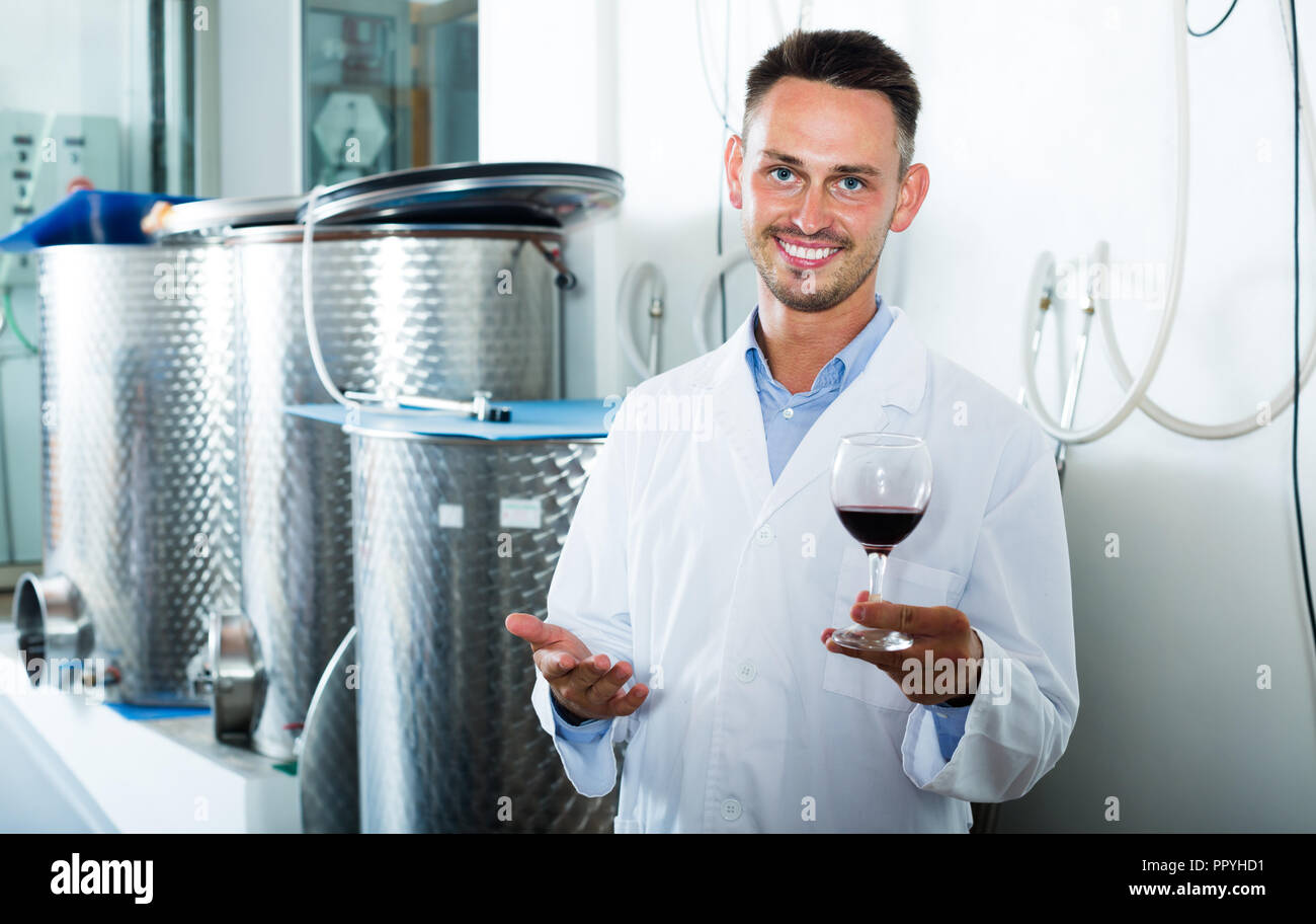 Happy winery worker wearing white coat holding glass of wine in ...