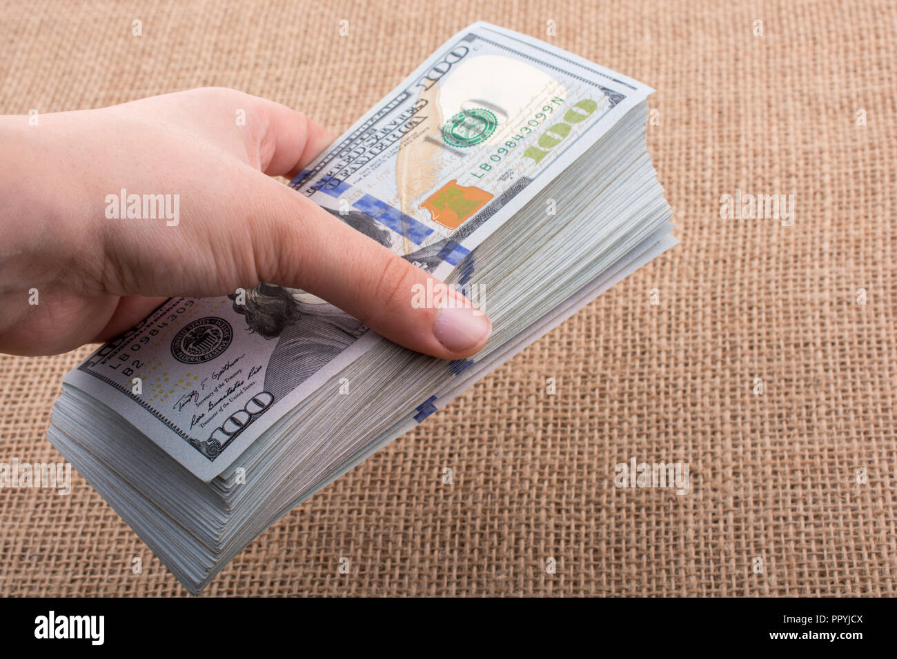 Hand holding banknote bundle of US dollar on a linen canvas background ...