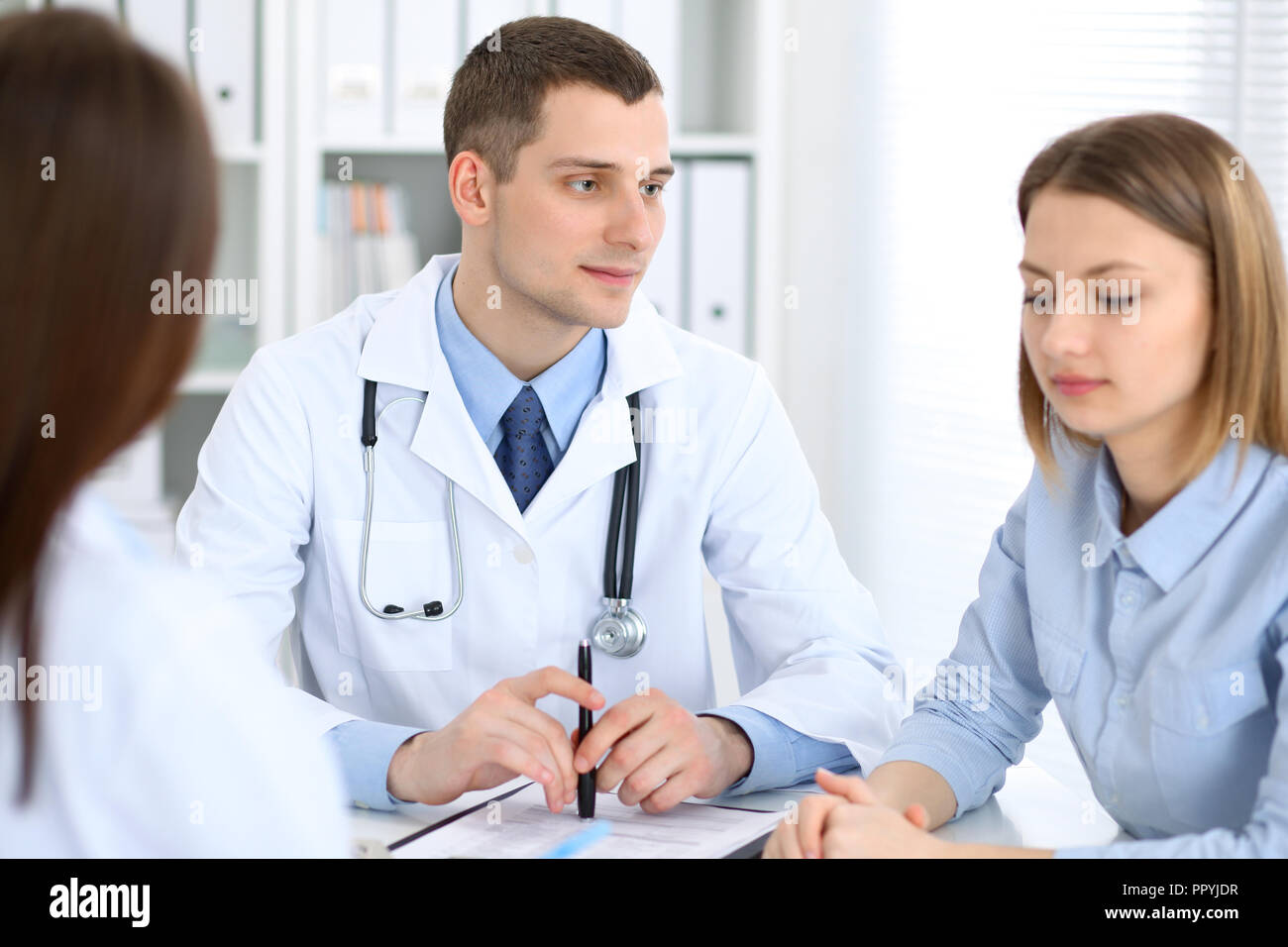 Two doctors and patient sitting at the table in medical cabinet. High ...