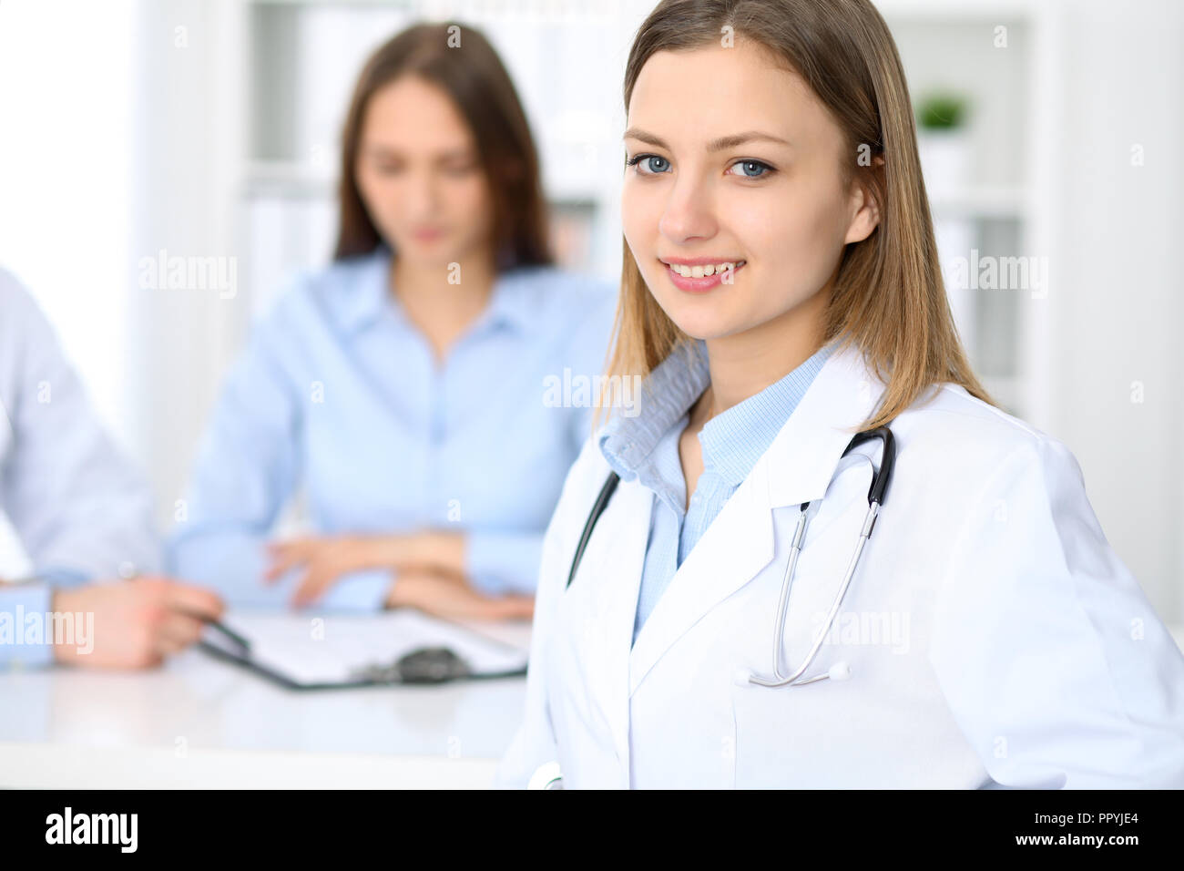 Young beautiful female doctor smiling on the background with patient in ...