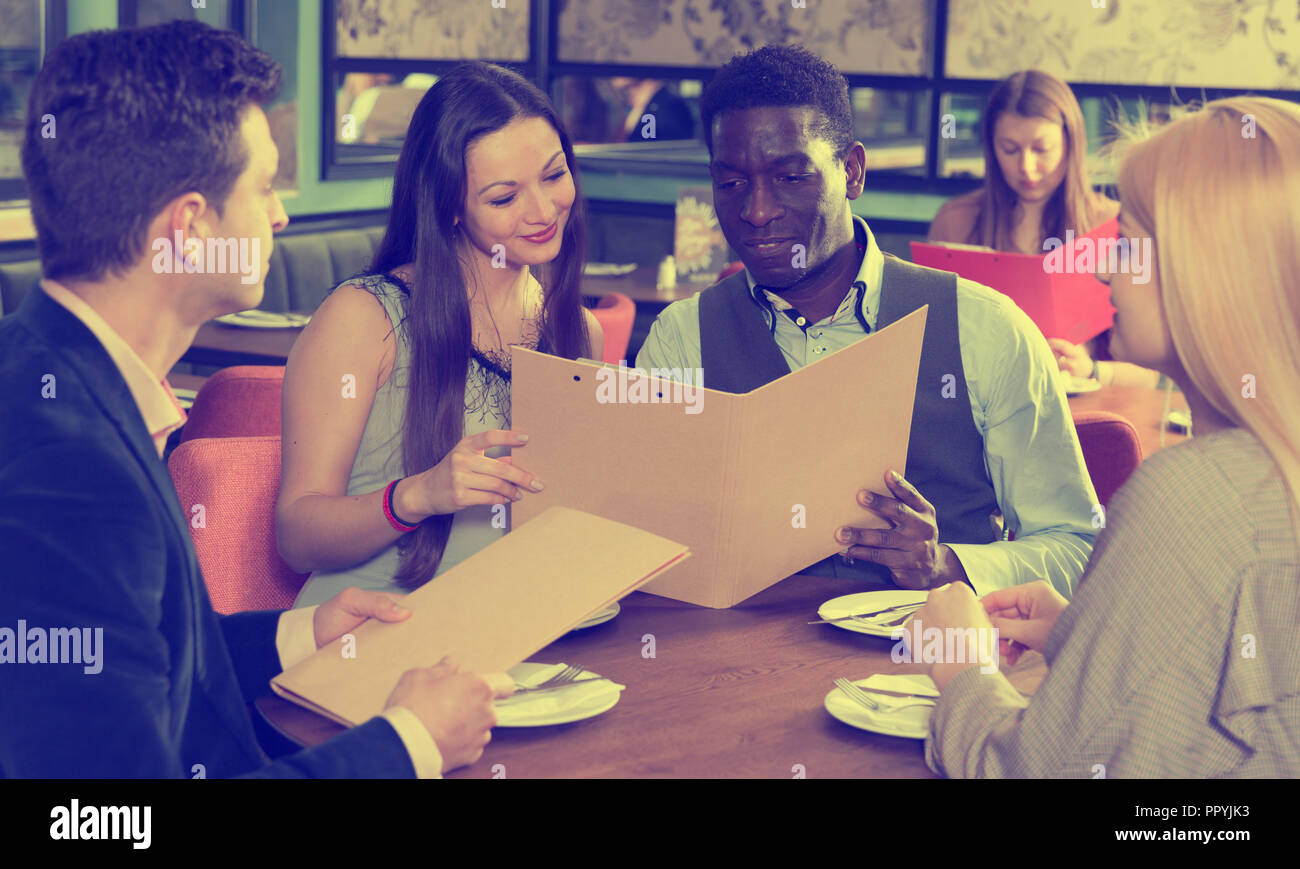 Сheerful friends choosing dishes from menu card in restaurant Stock ...