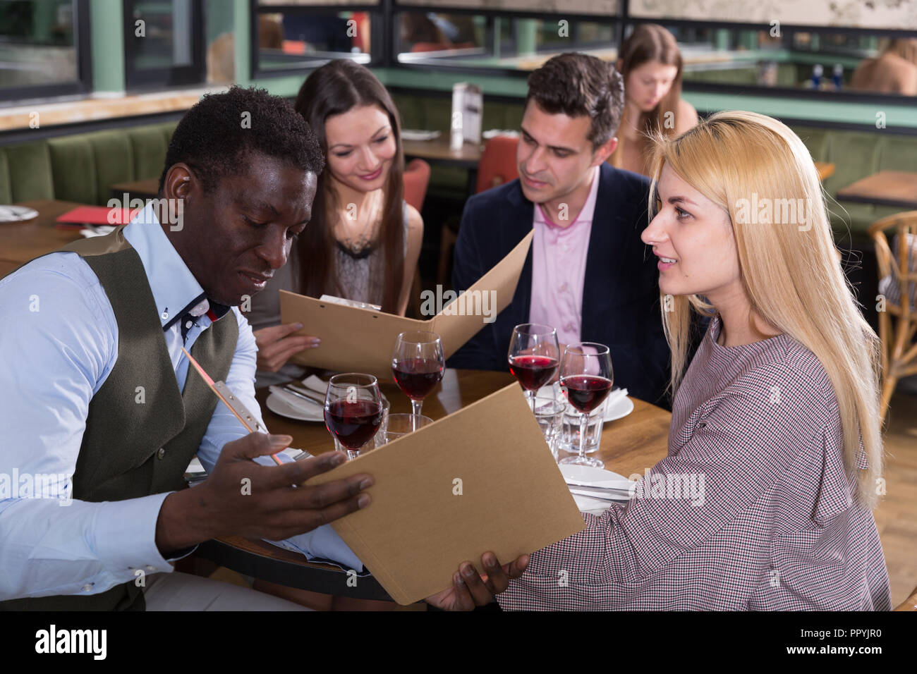 Сheerful friends choosing dishes from menu card in restaurant Stock ...