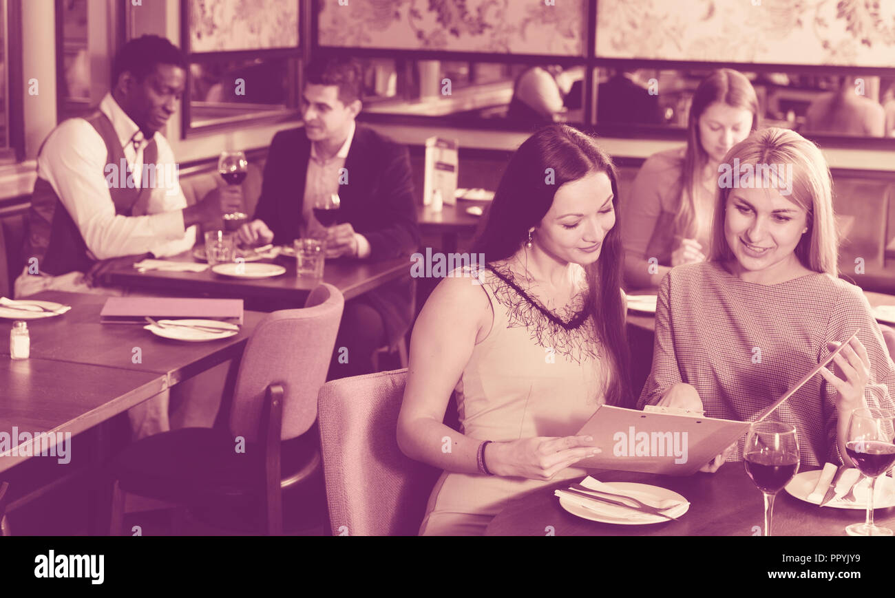Two young attractive female friends choosing dishes from menu card in ...