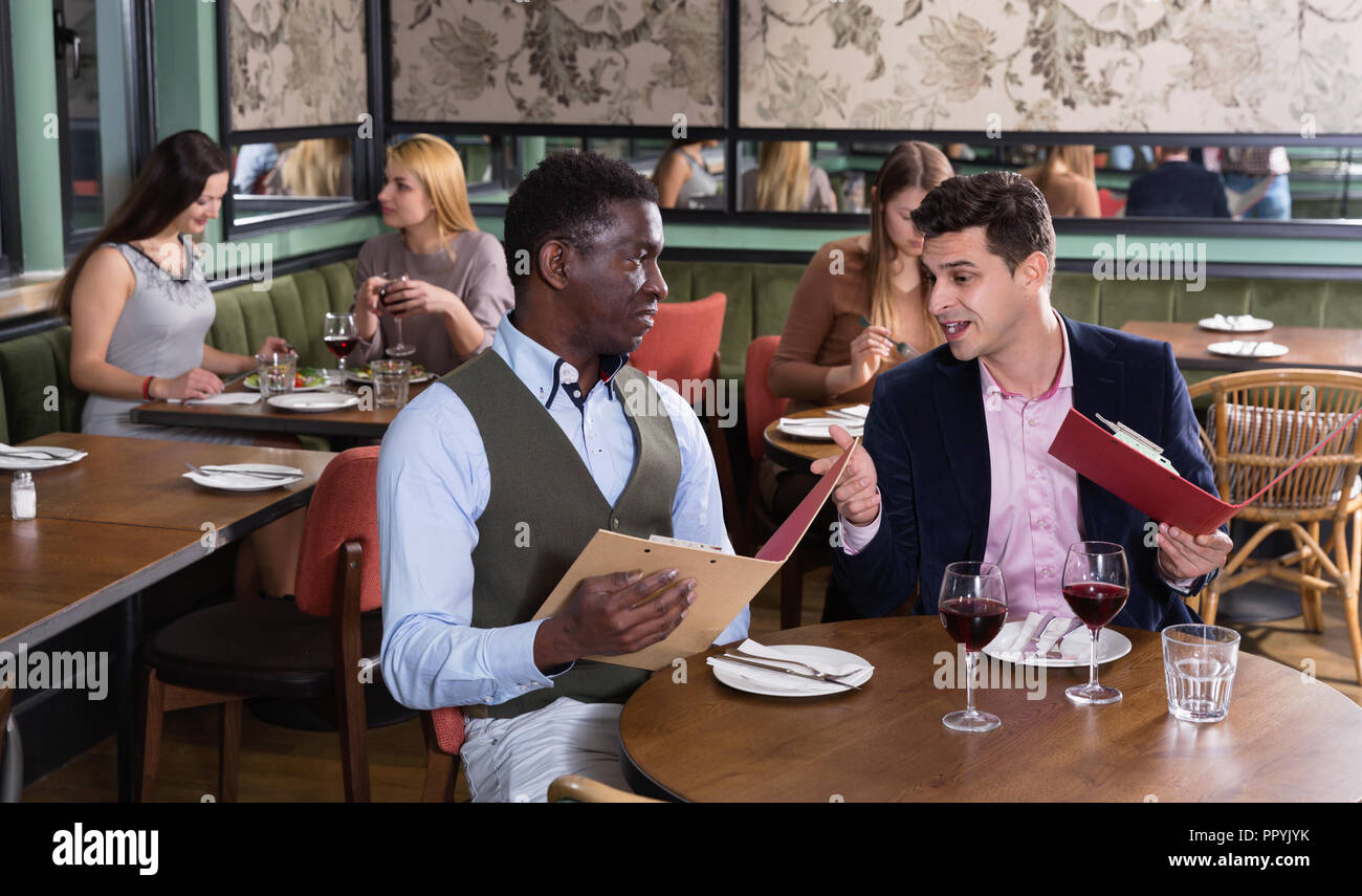 Сheerful positive smiling male friends choosing dishes from menu card ...