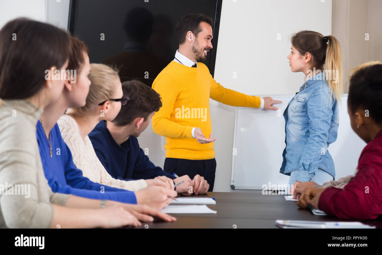 Young female student is giving answer to teacher’s question at writing ...