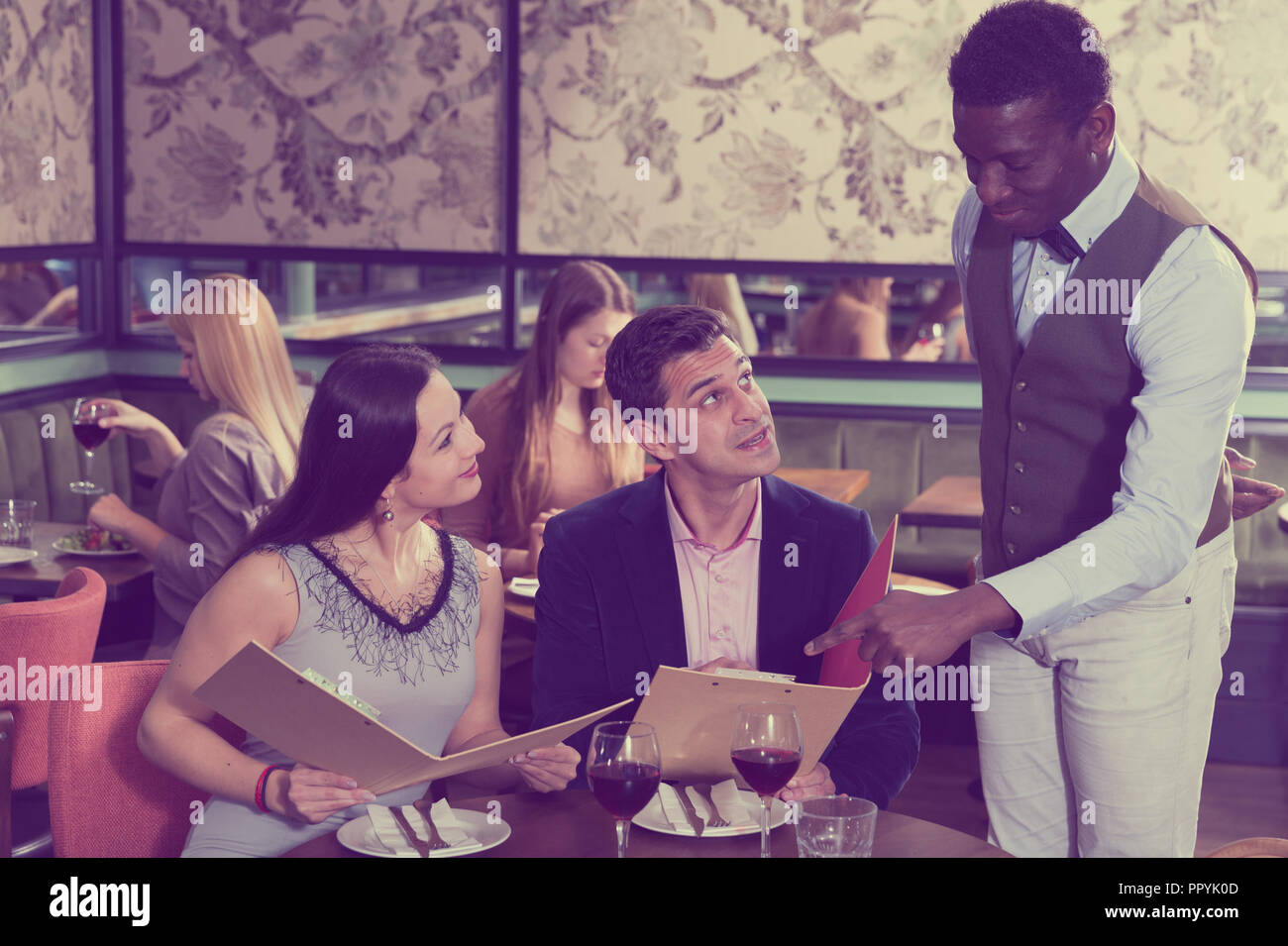 Smiling African American waiter taking order from couple, recommending ...