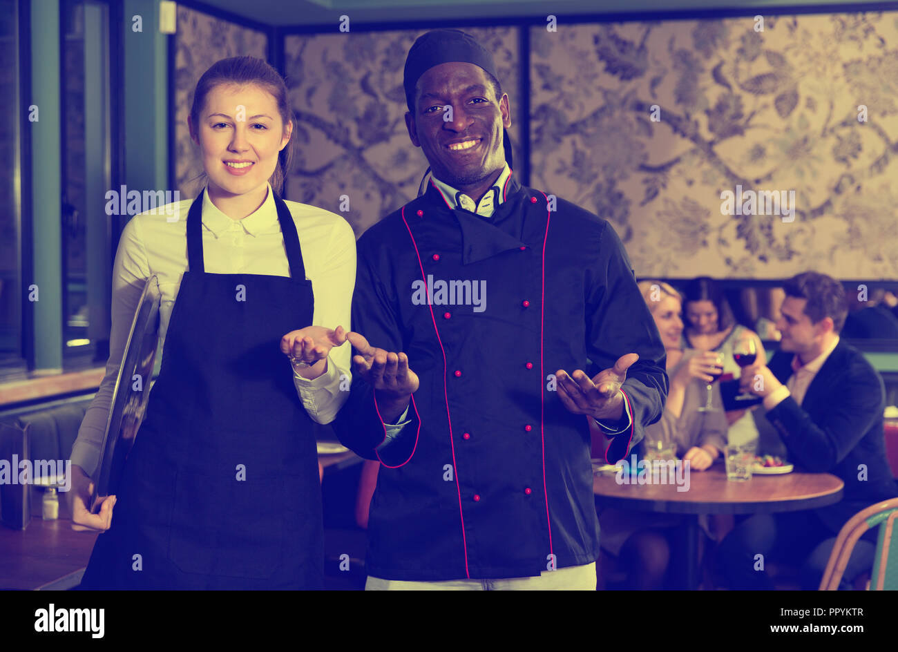 Polite happy cheerful waitress standing in restaurant hall with ...