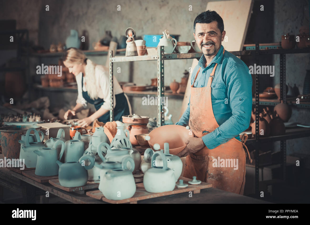 happy russian man and woman potters holding ceramic vessels in atelier ...