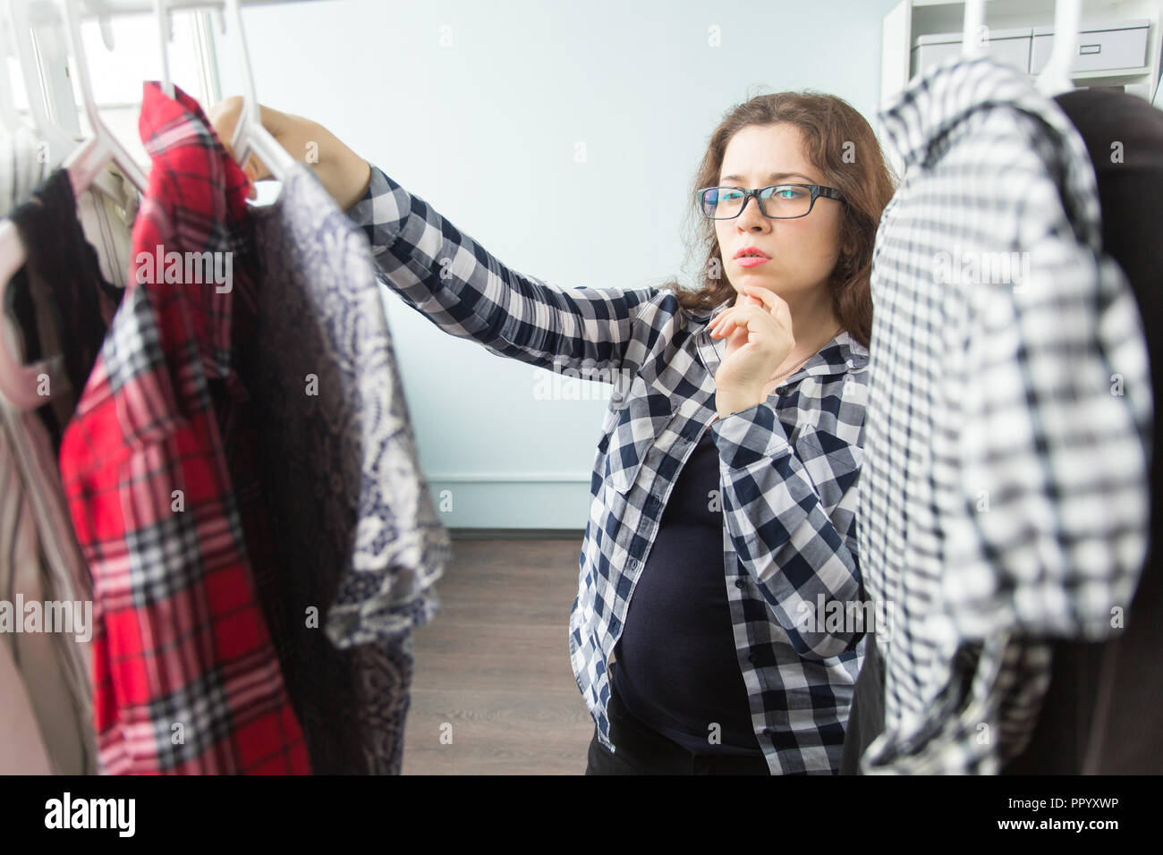 Clothes, fashion, people concept - serious young woman choosing clothes ...