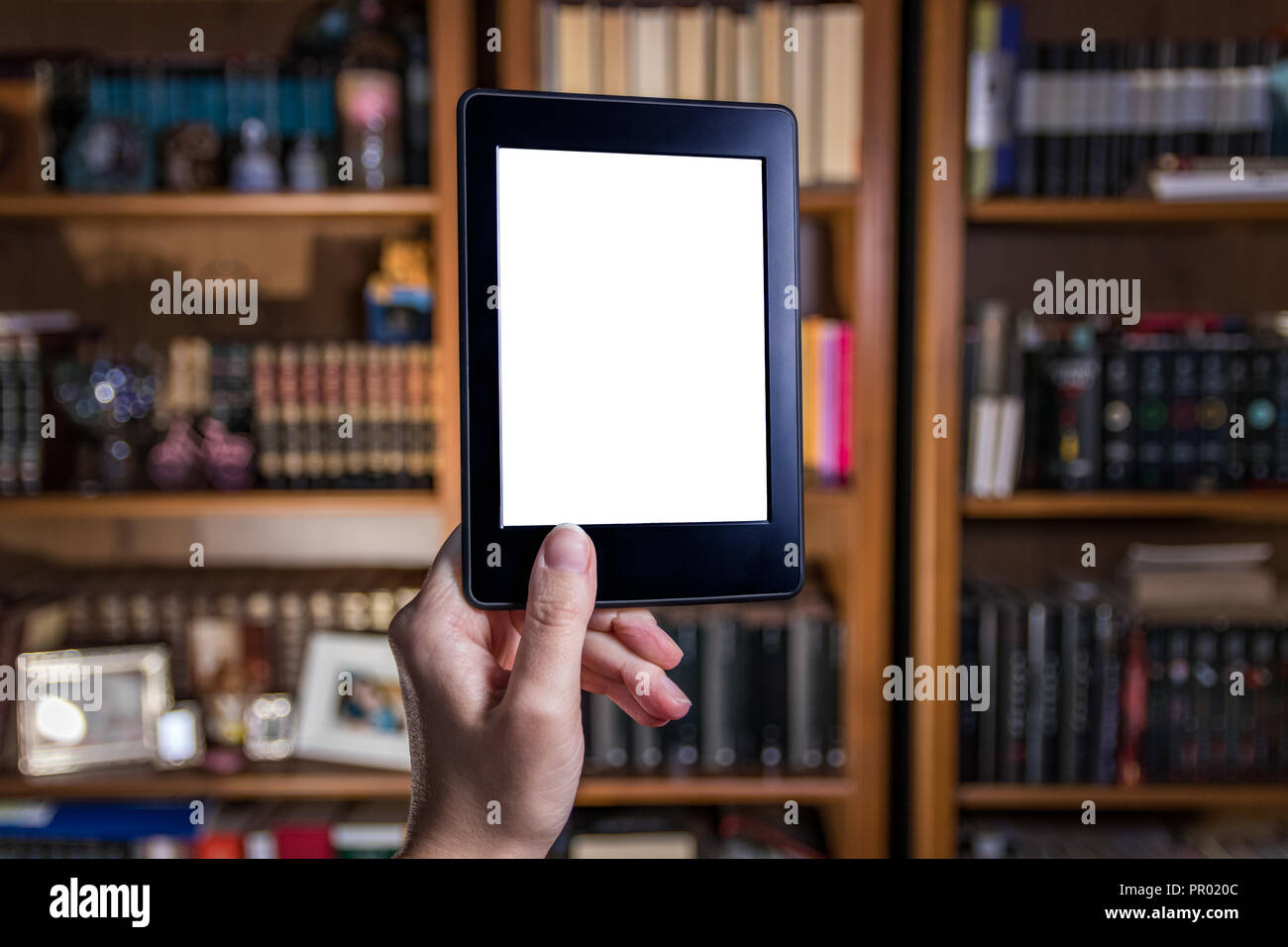 Womand hand holding e reader in front of bookshelves Stock Photo - Alamy