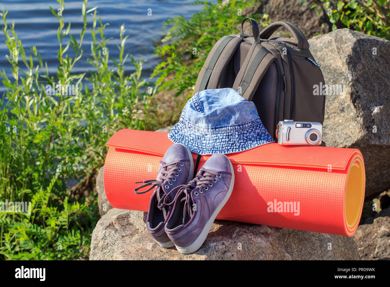 Hiking backpack, sneakers, hat, camera and camping mat on rock with ...
