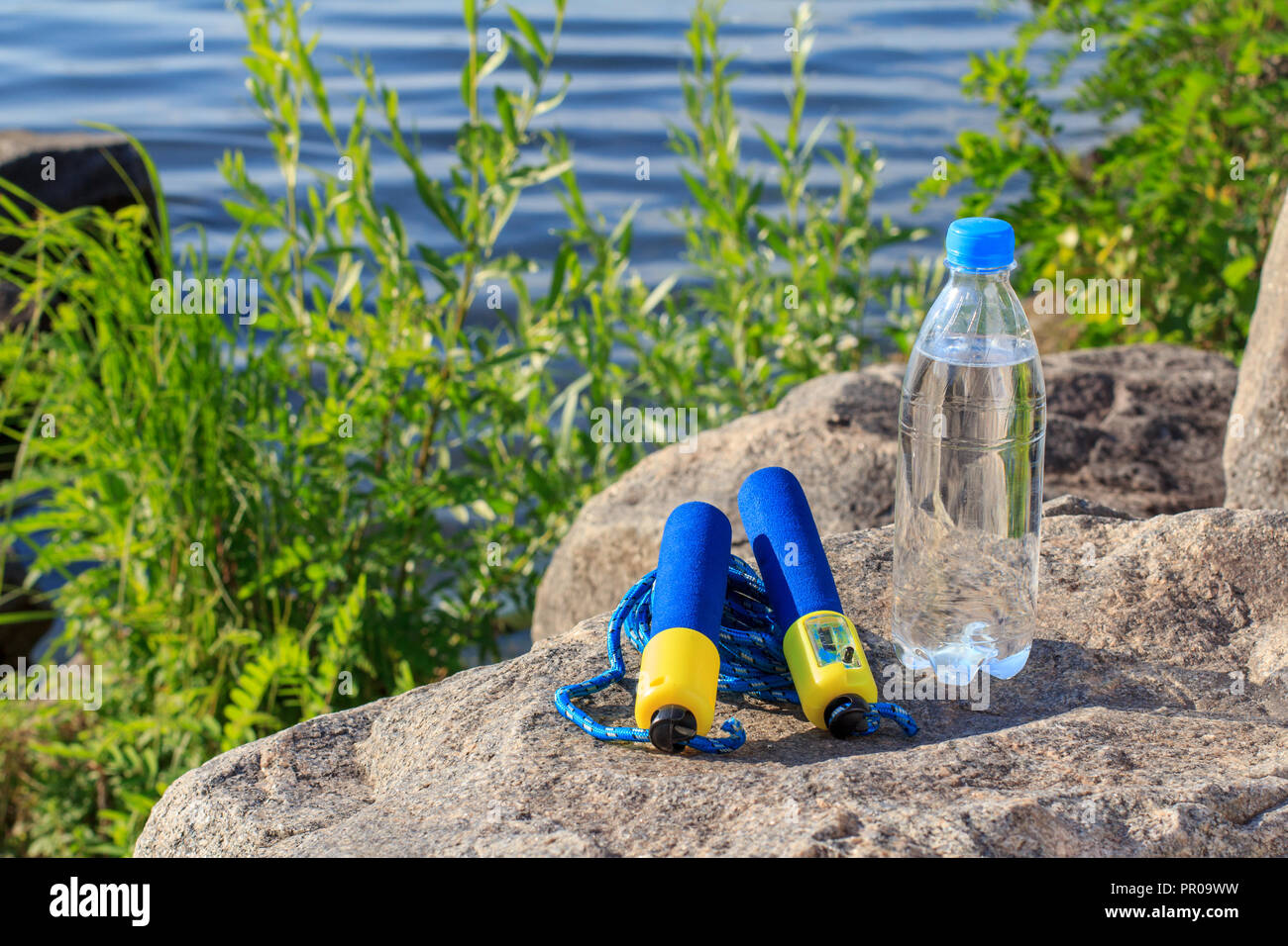 Jump rope and bottle with water on rock with river embankment ...