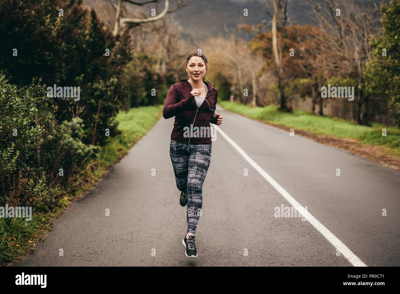 Portrait of fit young woman running on road in morning. Female jogging ...
