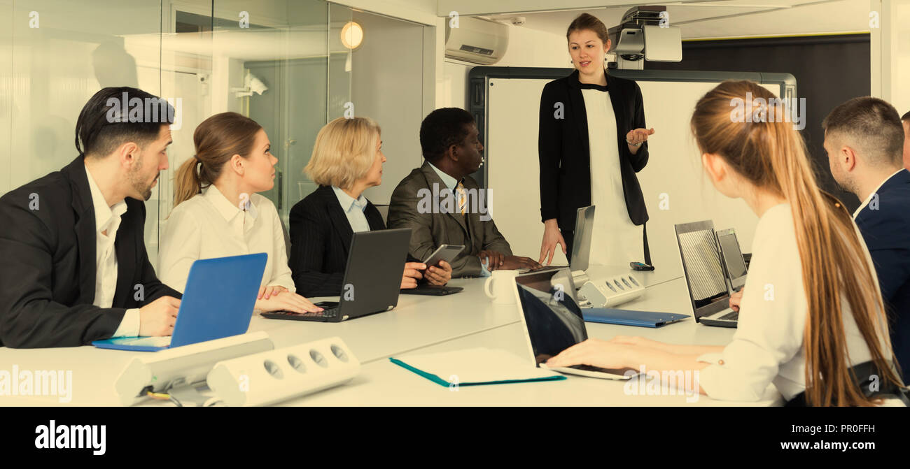 Young elegant girl making presentation to colleagues in modern meeting ...