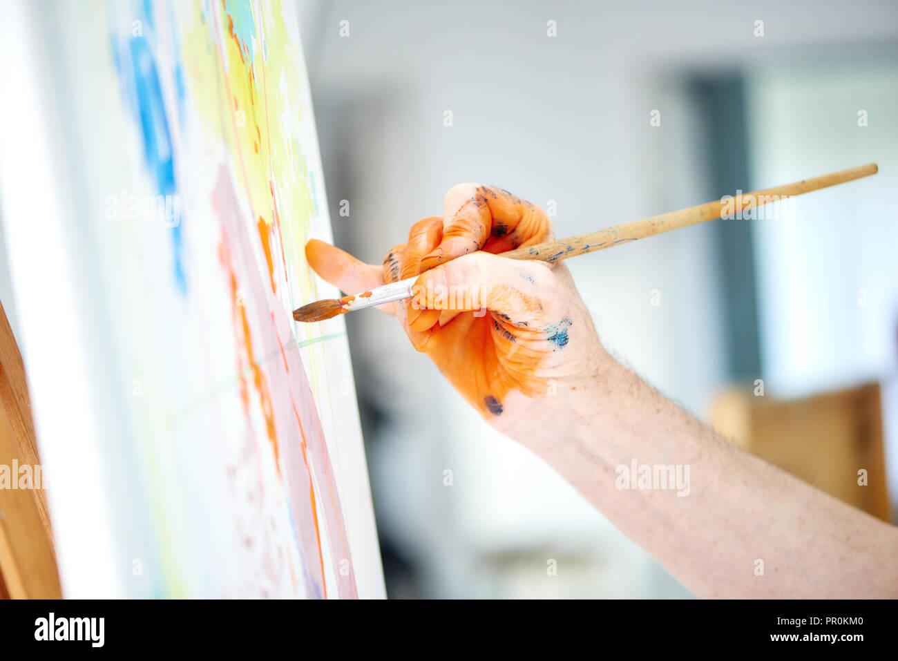 Close up of male artist hand, holding brush and painting rich orange ...