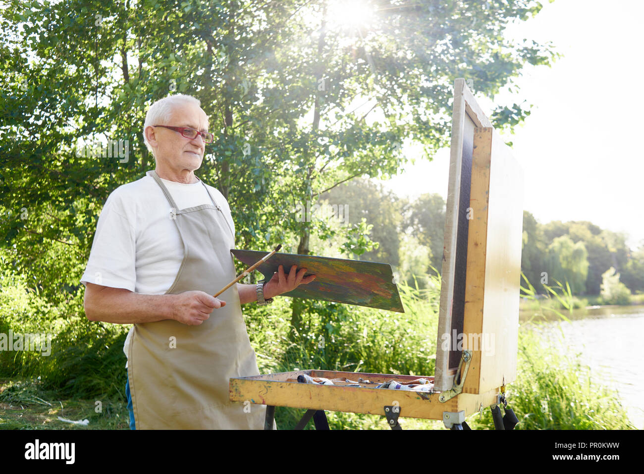 Senior male painter, standing with painting brush and palette of colors ...