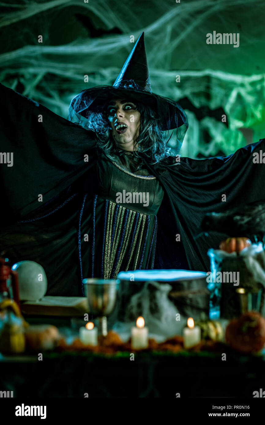 Witch with awfully face and hat on her head in creepy surroundings and ...