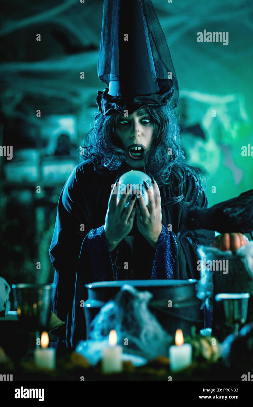 An angry witch is watching the future in magic ball above the pot with ...