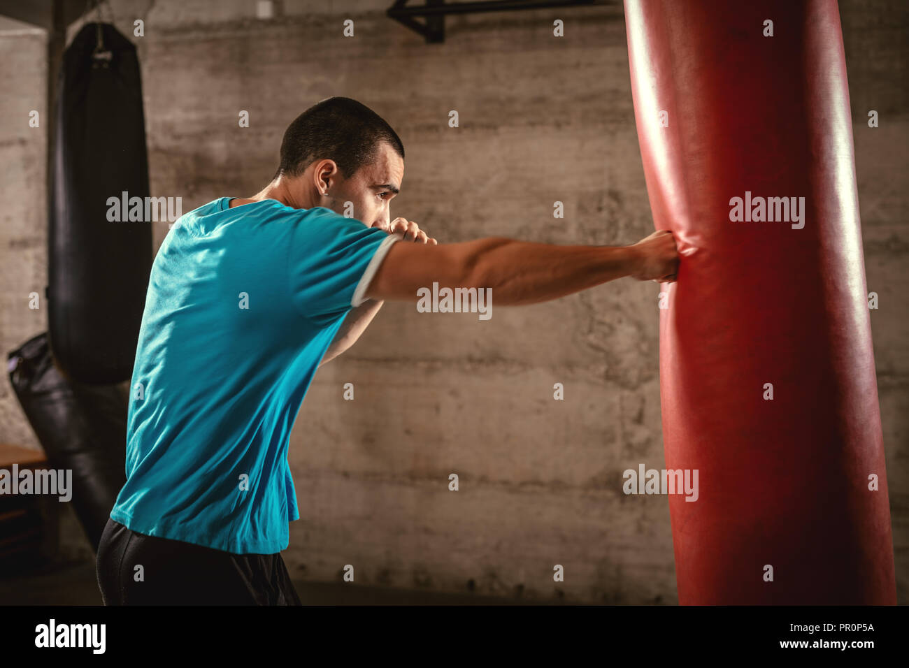 Young muscular man punching a boxing bag on cross fit training at the ...