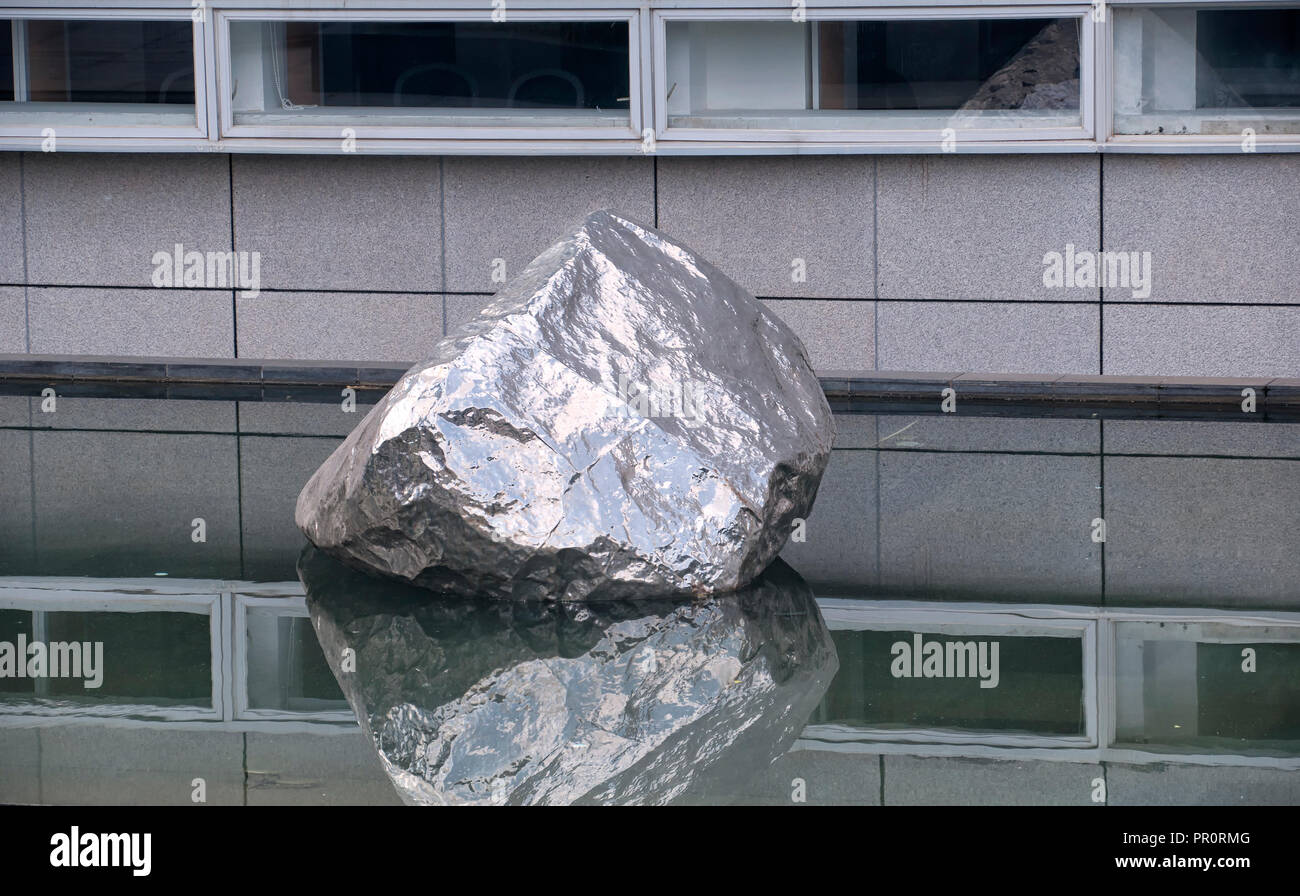 A silver rock reflecting on water at a museum in Shenzhen China in the ...