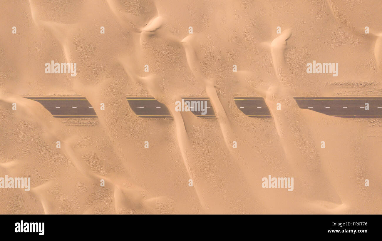 Aerial view of a desert road being run over by sand dunes photographed ...