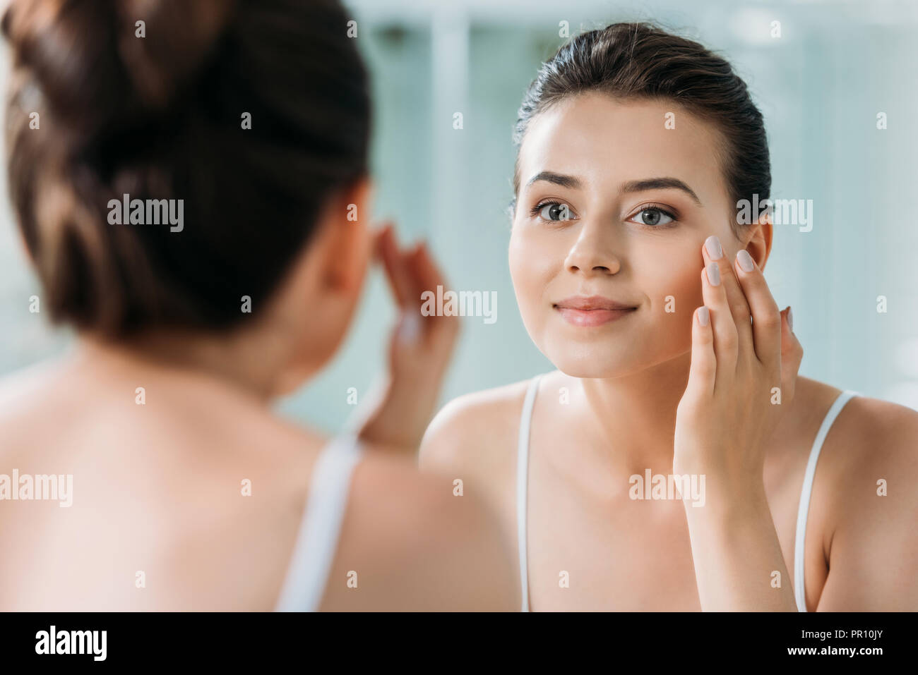 Beautiful Smiling Girl Touching Face And Looking At Mirror In Bathroom